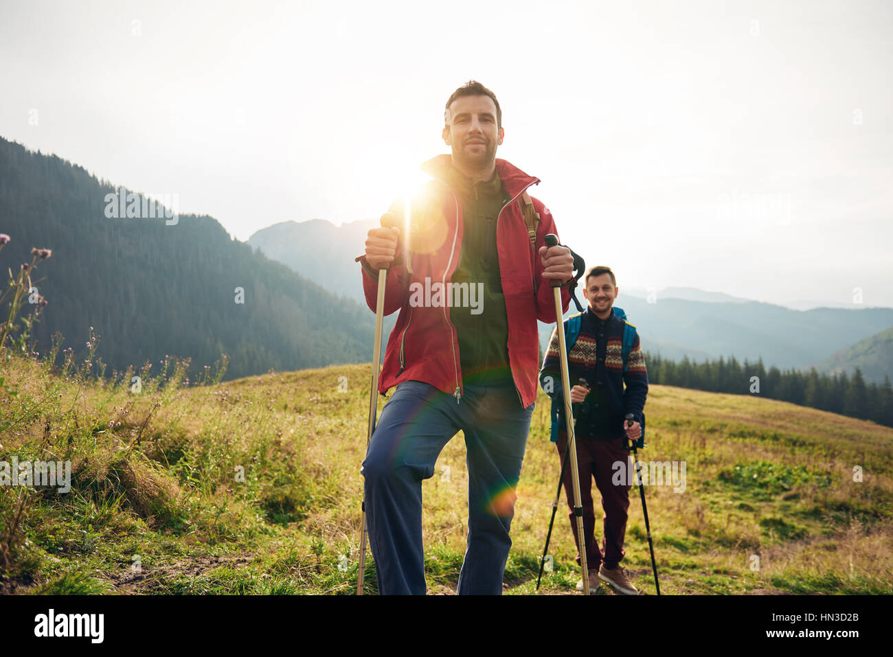 Portrait of two young men wearing backpacks and carrying trekking poles ...