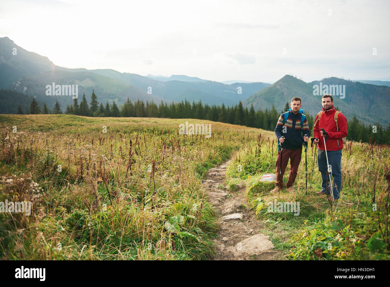 Portrait of two young men wearing backpacks and carrying trekking poles ...