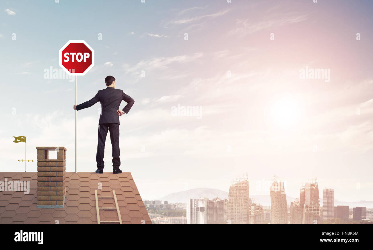 Businessman standing on house roof and holding stop sign. Mixed media ...