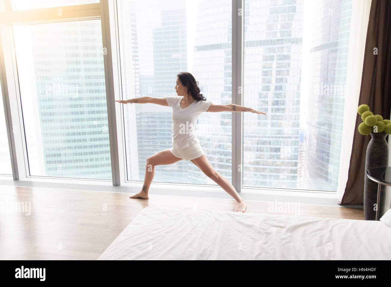 Young attractive woman in Warrior 2 pose, sunny floor window Stock ...