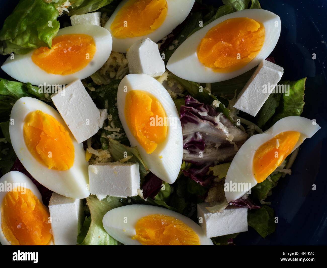 High angle view of green salad wth boiled eggs and feta cheese in blue ...