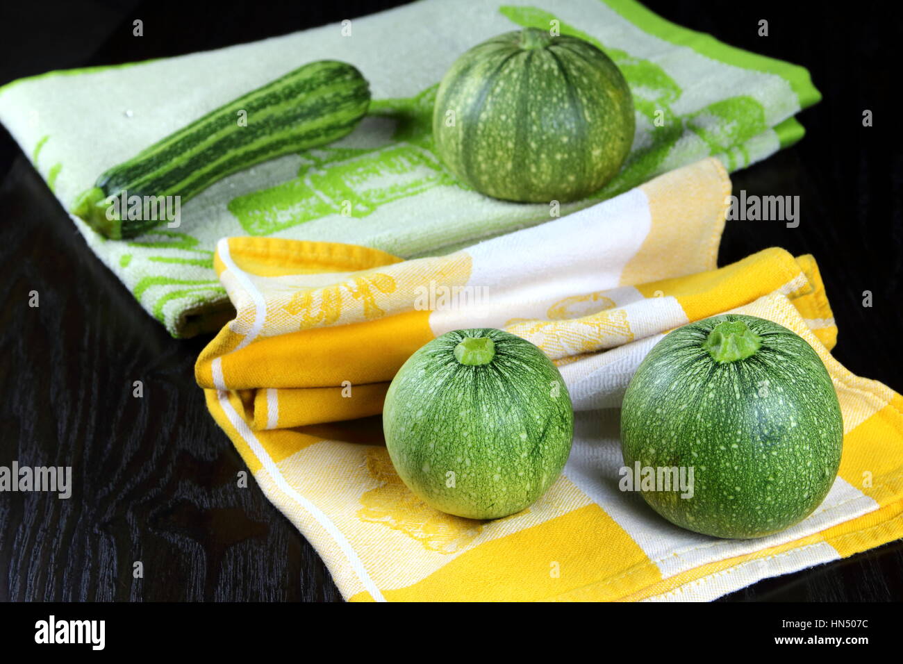 Round zucchini and striped courgette on colorful kitchen cloths lying ...