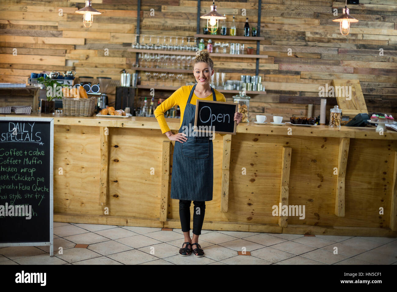Portrait of smiling waitress standing with open sign board in cafe ...