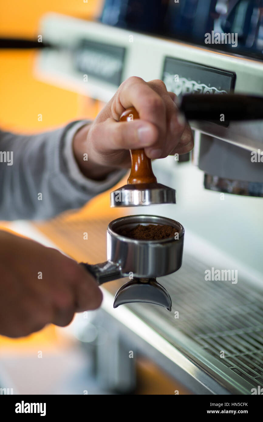 Waiter using a tamper to press ground coffee into a portafilter in ...
