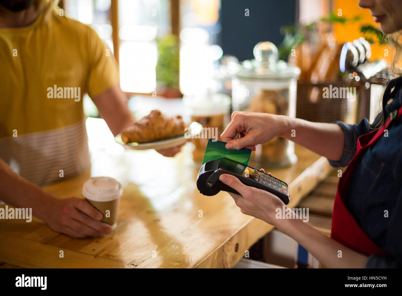 Mid-section of customer making payment through credit card at counter ...
