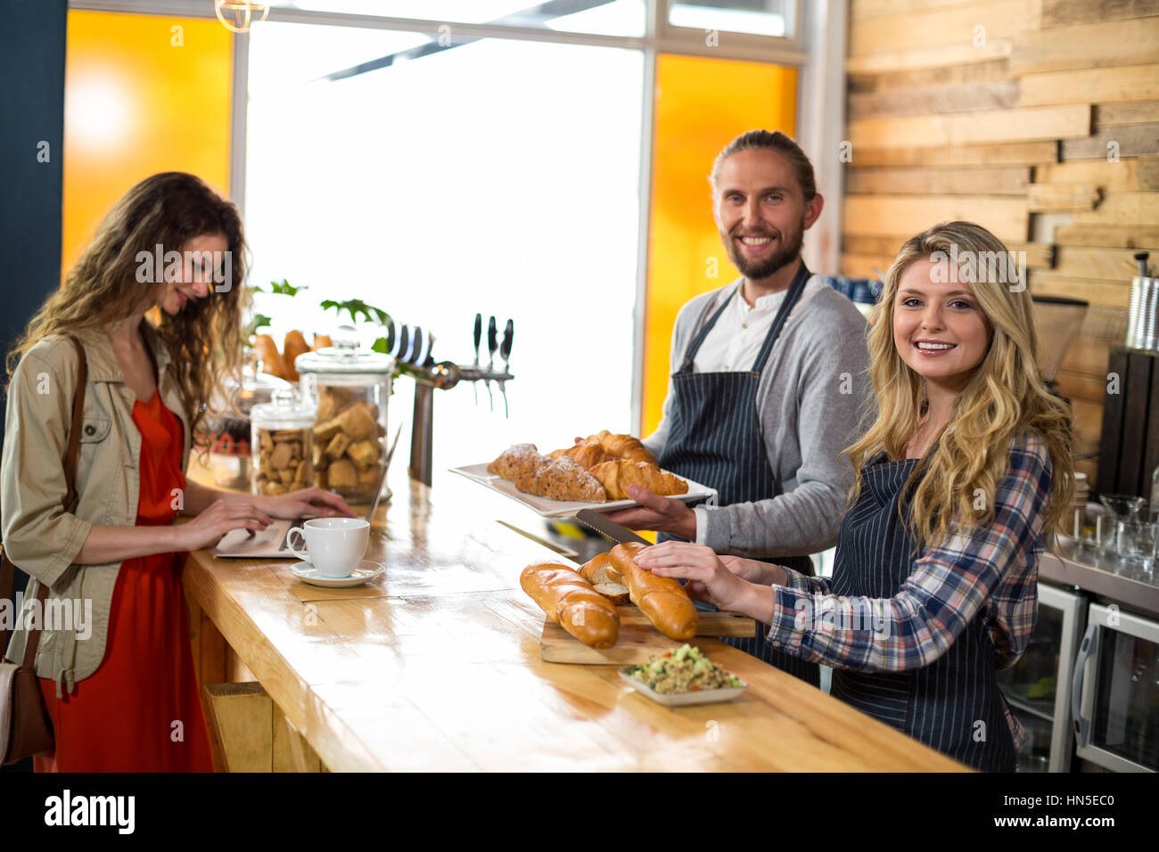 Woman using laptop and waiter cutting bread at counter in cafÃƒÂ© Stock ...