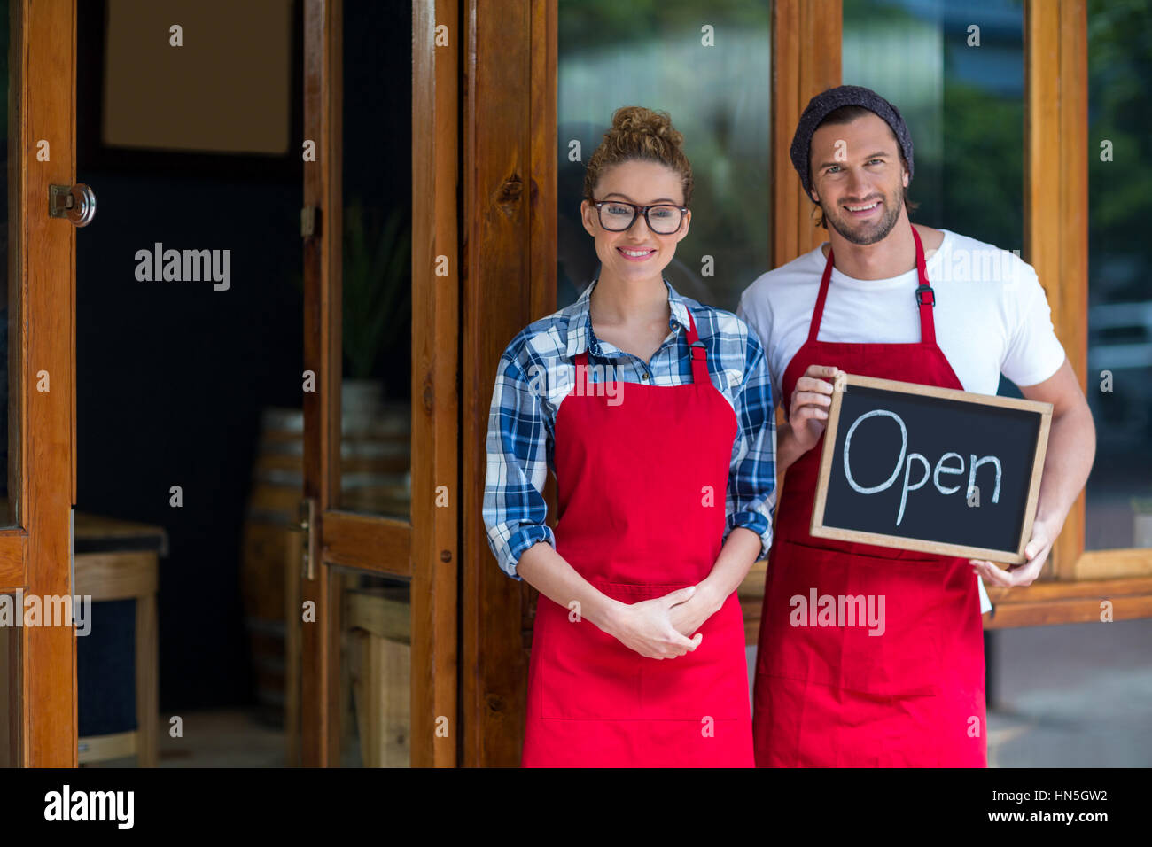 Portrait of smiling waitress and waiter standing with open sign board ...