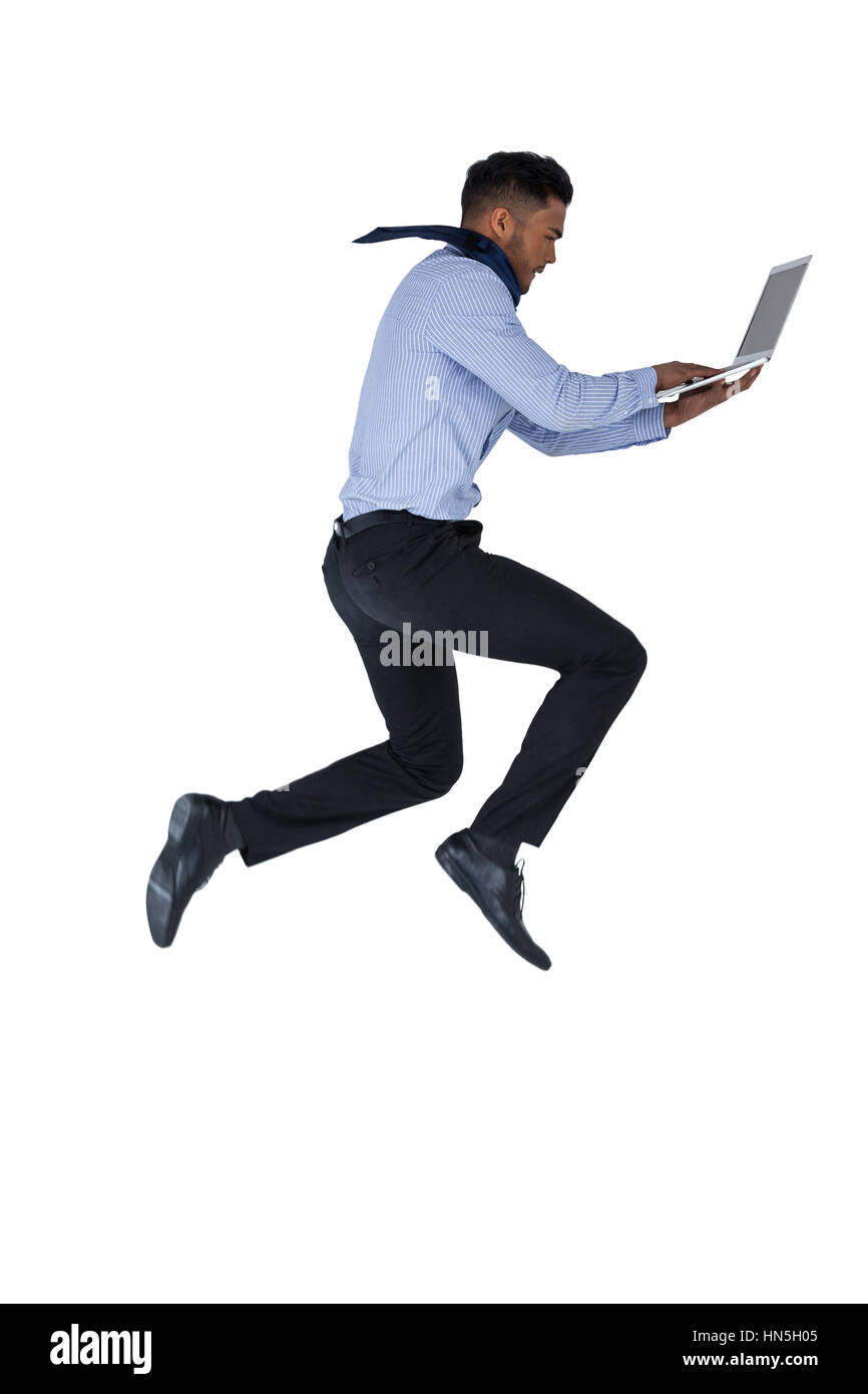 Businessman jumping while using laptop against white background Stock ...