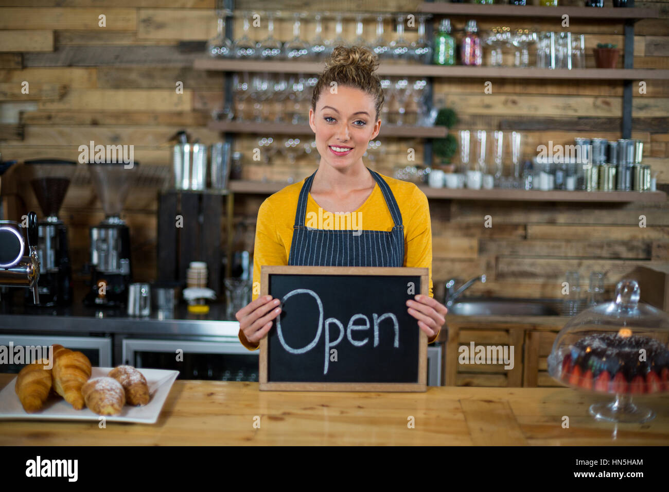 Portrait of smiling waitress standing with open sign board in cafe ...