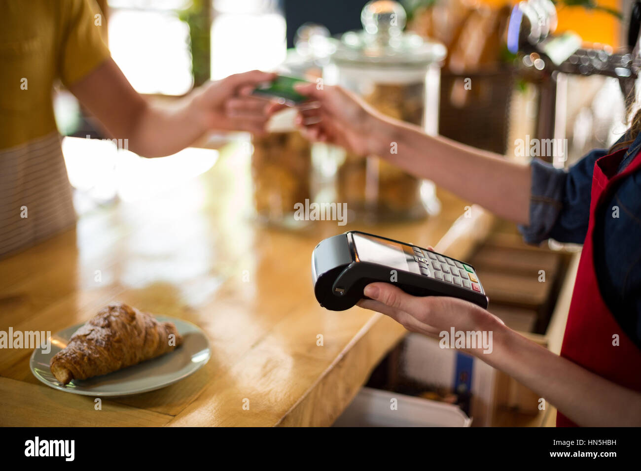 Mid-section of customer making payment through credit card at counter ...