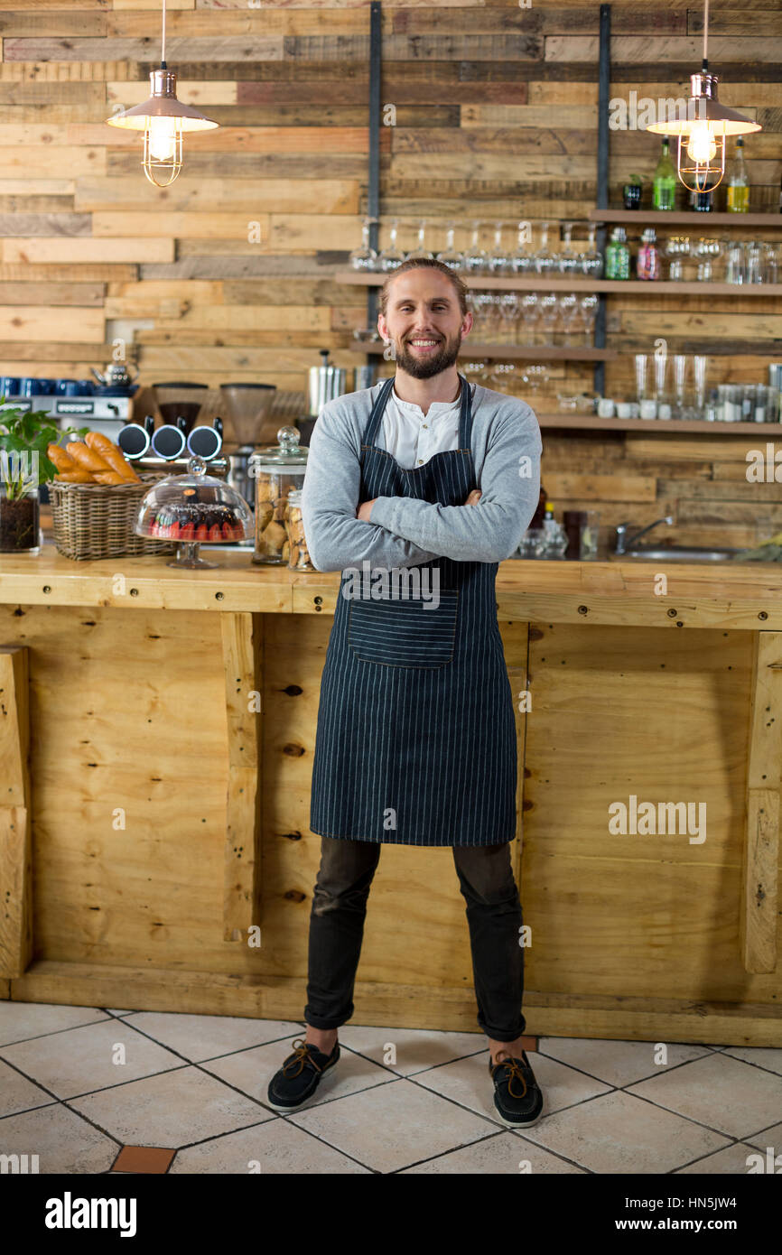 Portrait of waiter standing with arms crossed at counter in cafÃƒÂ ...