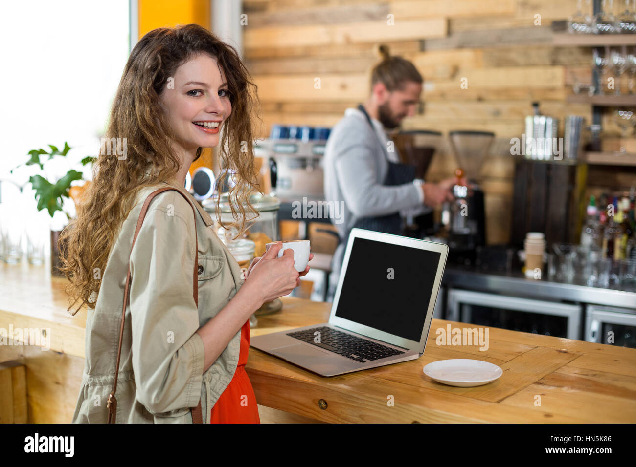 Portrait of woman standing at counter and using laptop while having ...