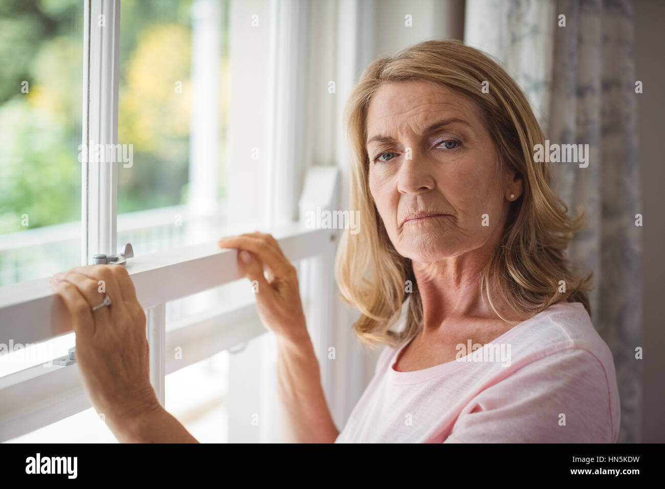 Portrait of senior woman standing next to window at home Stock Photo ...