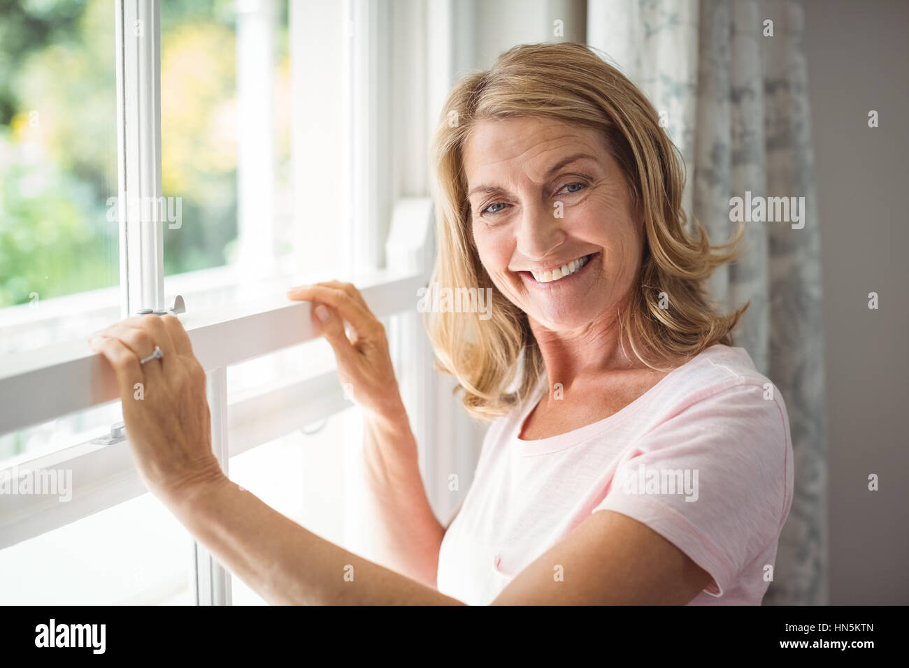 Portrait of happy senior woman standing next to window at home Stock ...