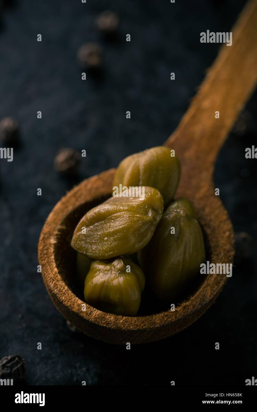 Vertical photo of pickled green capers. Few pieces of edible blooms are ...