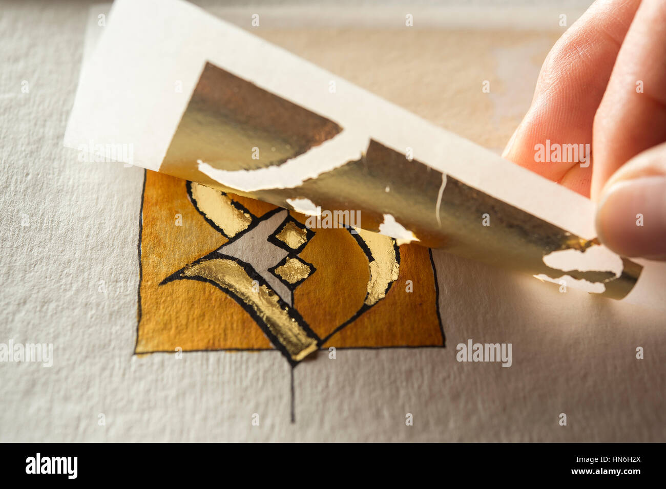 Calligraphy studio, hand removing sheet of transfer gold, letters S ...