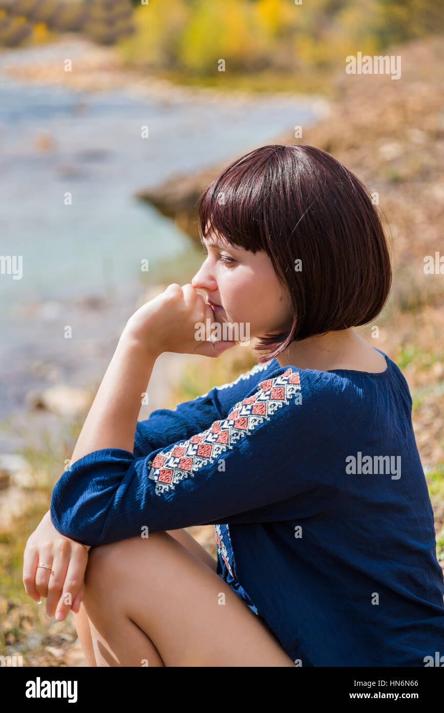 Young woman sitting contemplating by light green creek during autumn ...