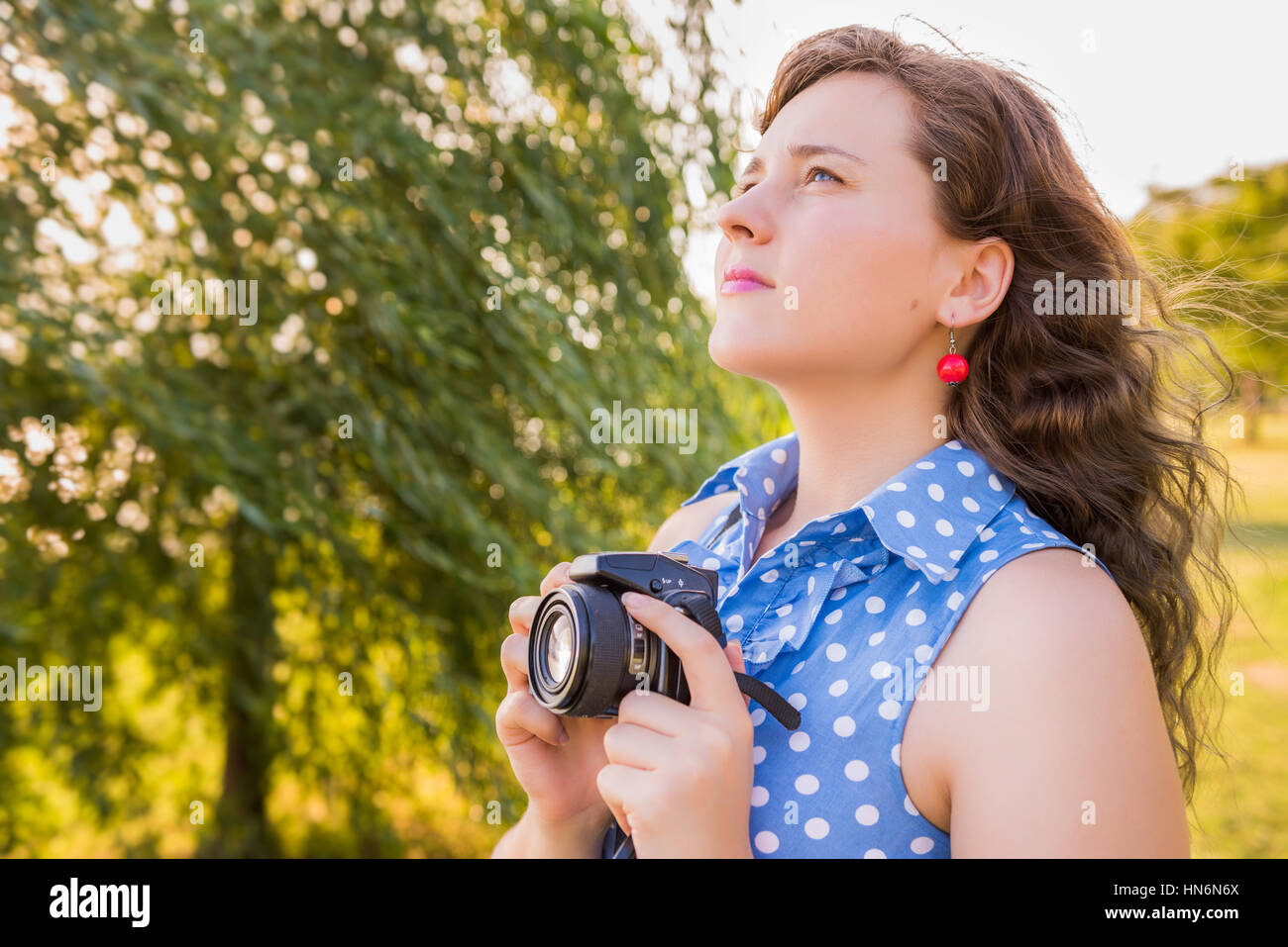 Side profile view of young woman photographer holding camera in green ...