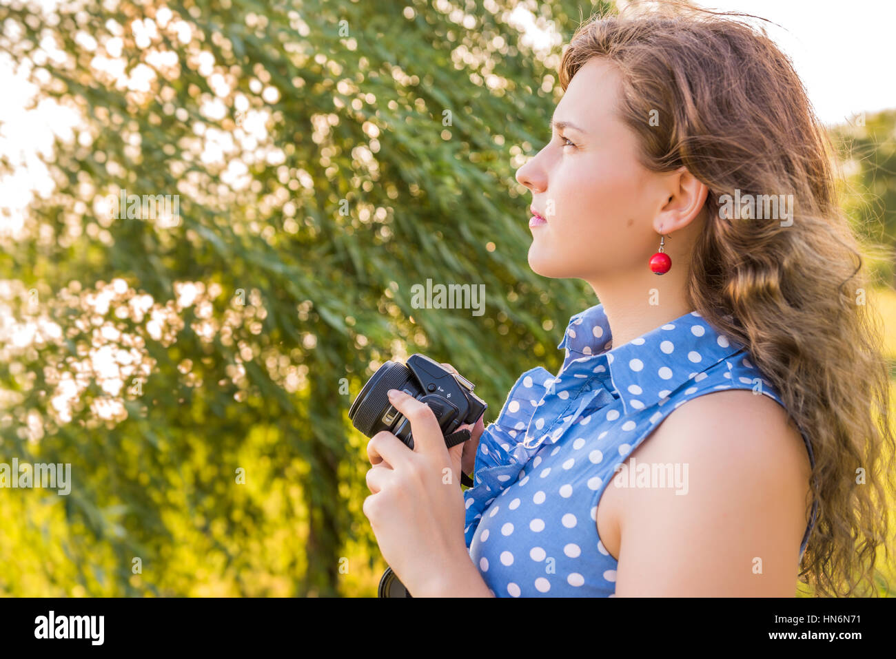 Side profile view of young woman photographer holding camera in green ...