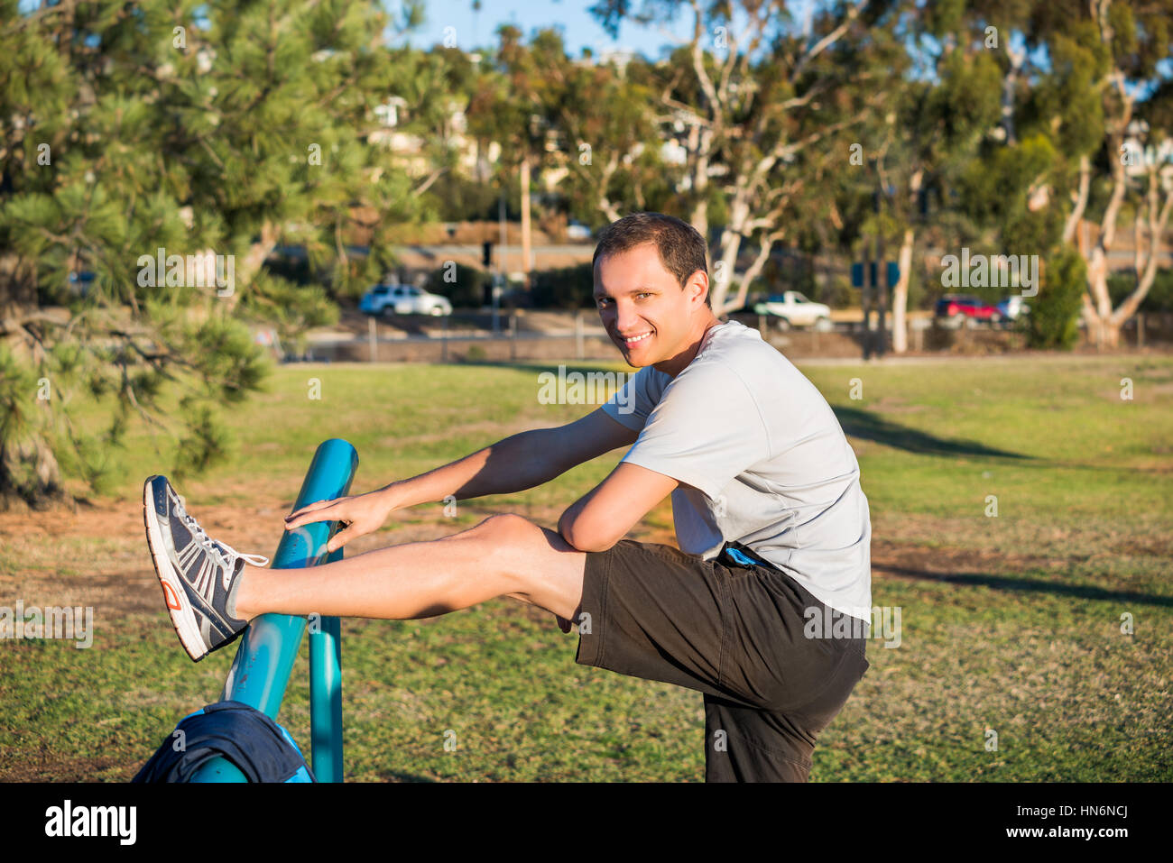Fit man smiling and stretching during workout on bar in outdoor green ...