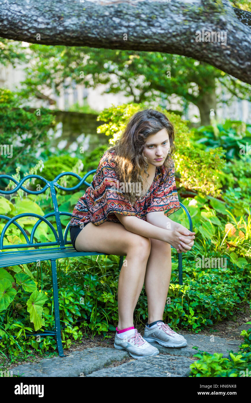 Young sad woman sitting on bench in garden thinking Stock Photo - Alamy