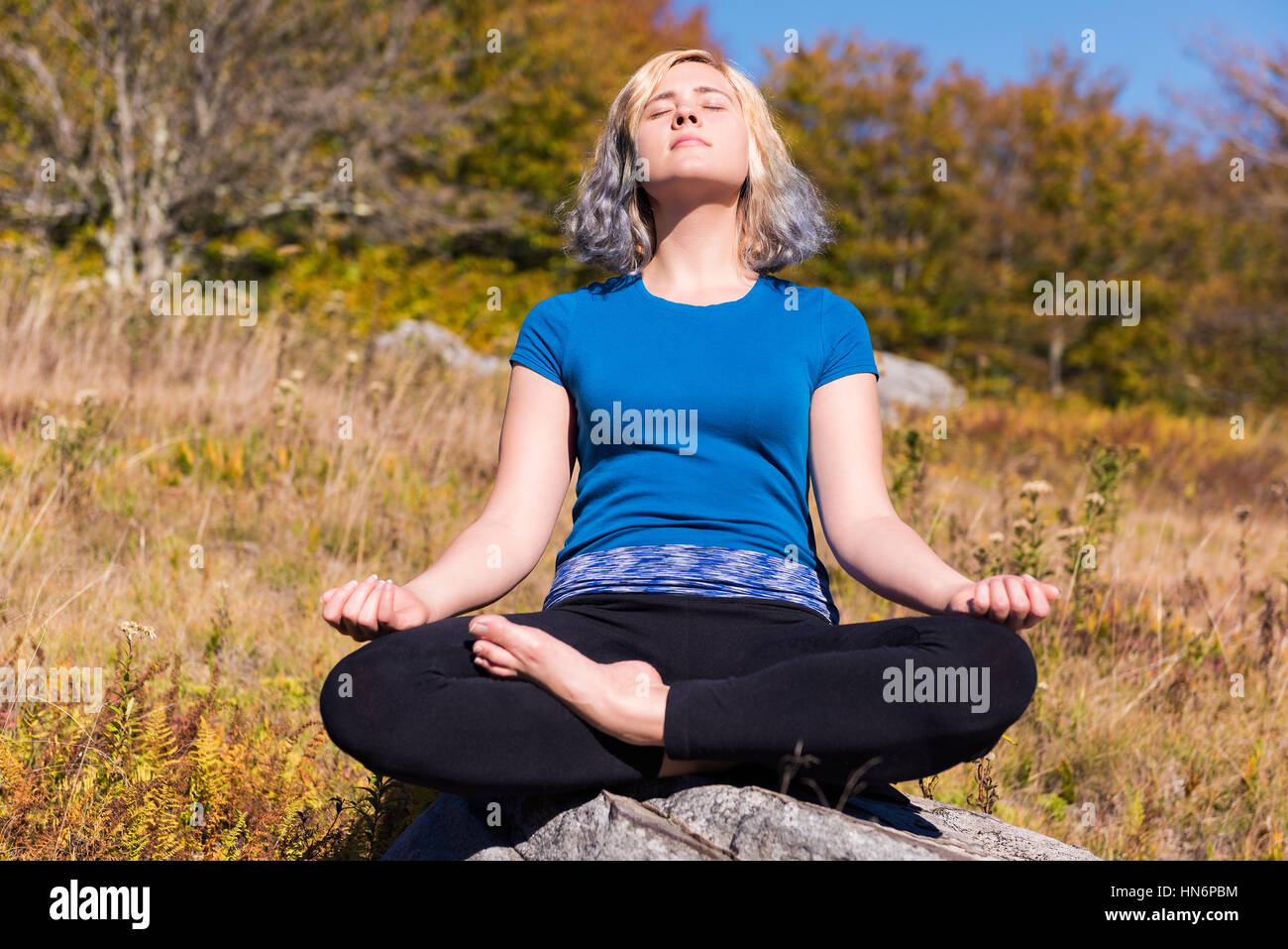 Young woman meditating sitting on rock cross legged in field in yoga ...