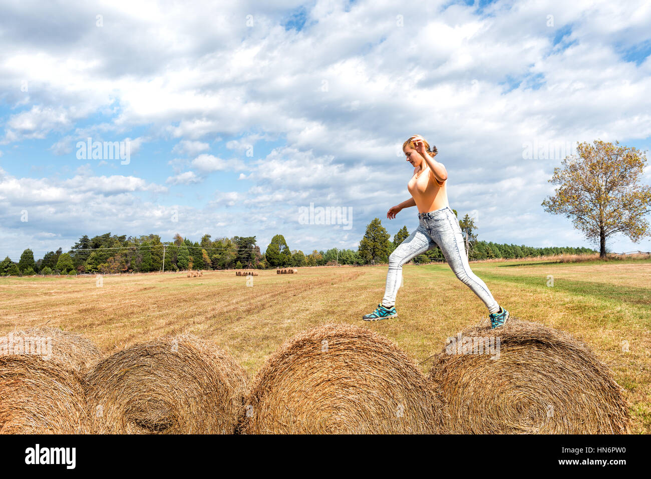 Young woman jumping over hay roll bales in a field Stock Photo - Alamy