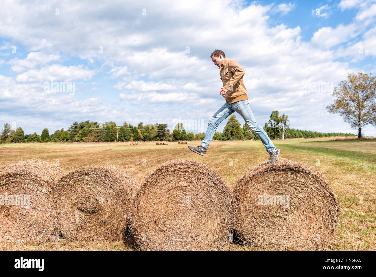 Young man jumping over hay roll bales in a field Stock Photo - Alamy