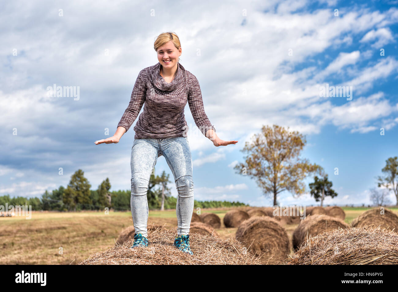 Young woman balancing on hay roll bale Stock Photo - Alamy