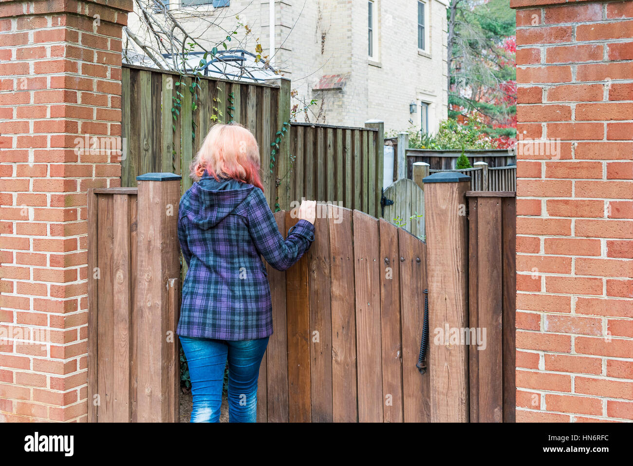 Back of young woman opening wooden fence door in neighborhood in autumn ...