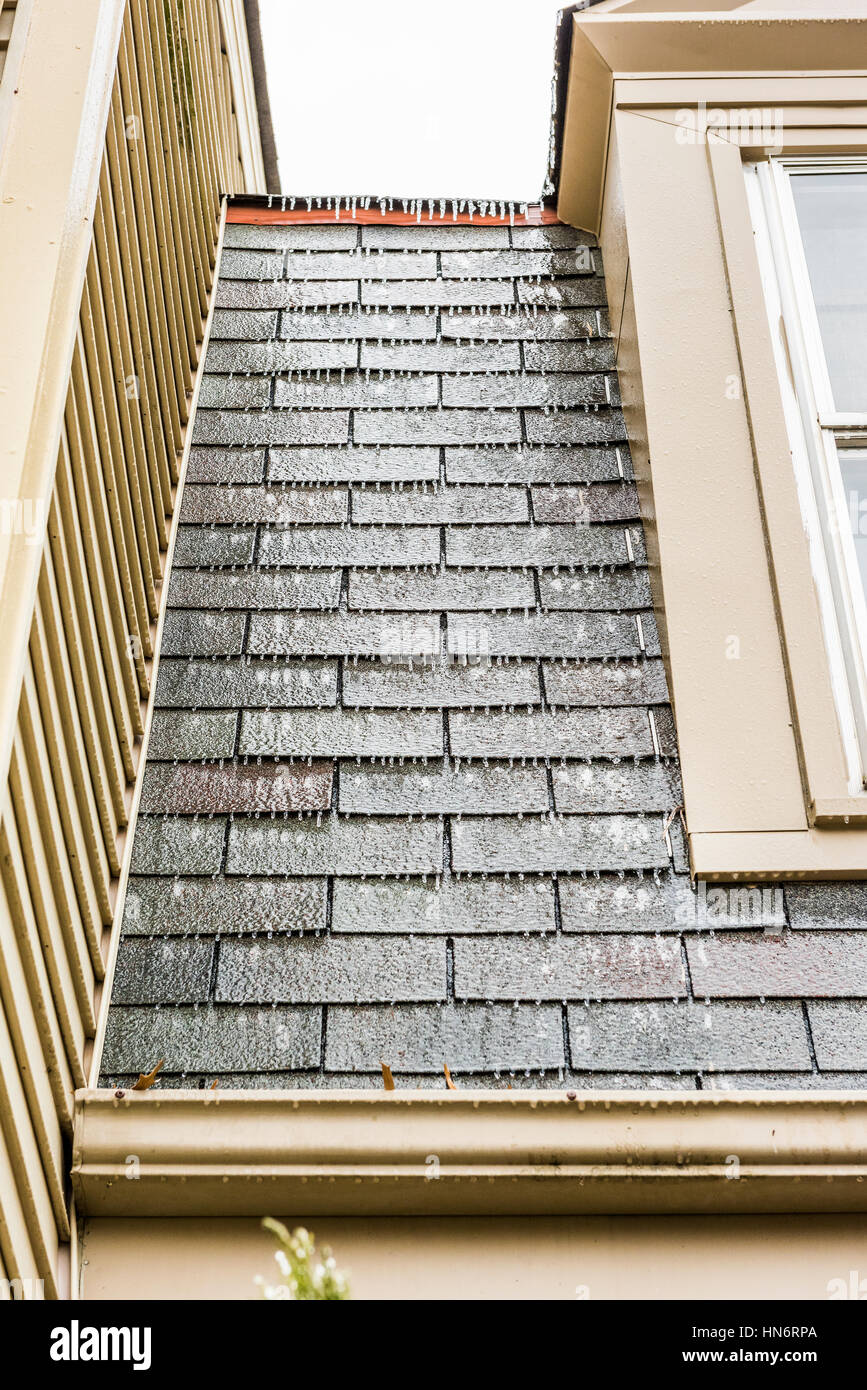 Icicles hanging on house roof shingles Stock Photo - Alamy