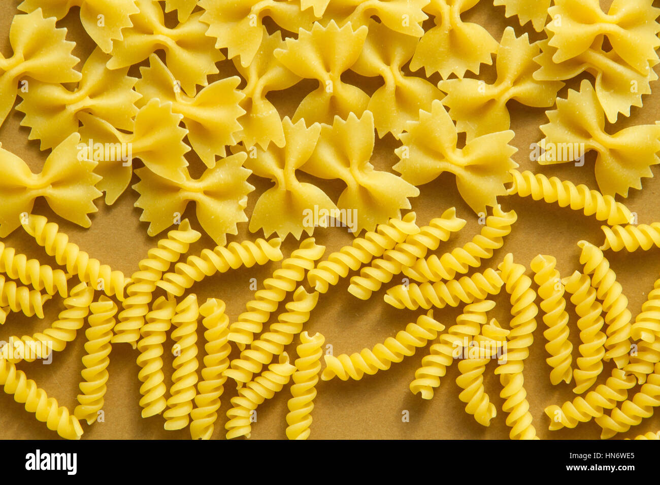 Bow and spiral shape pasta on brown background close view Stock Photo ...