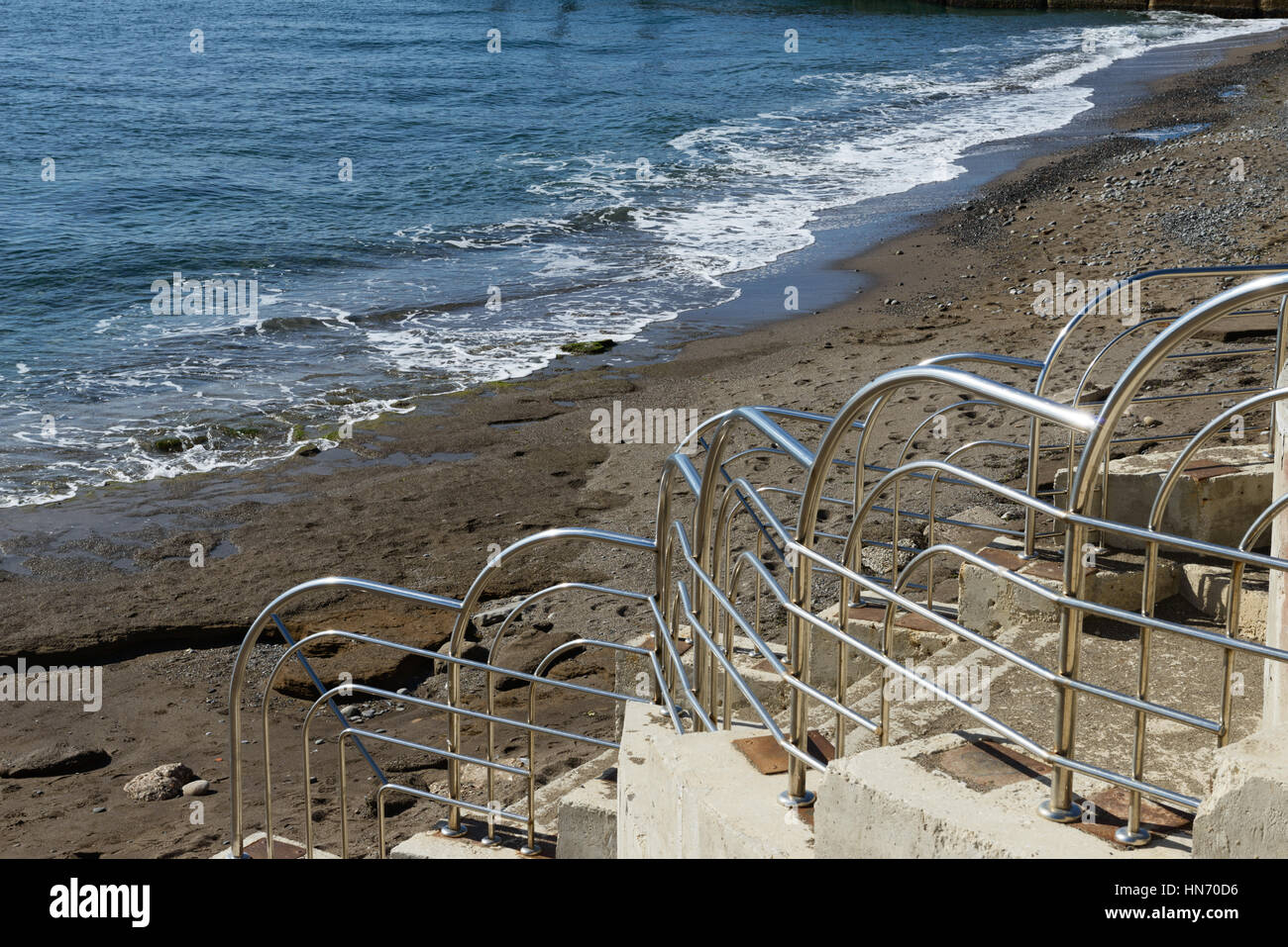 Shiny metal handrail of beach stair on background of sand and splashing ...