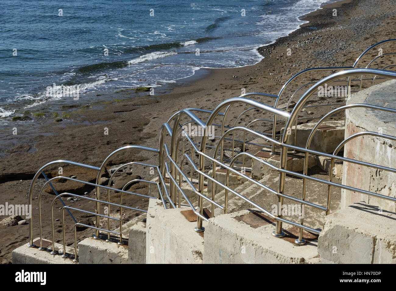 Shiny metal handrail of beach stair on background of sand and splashing ...