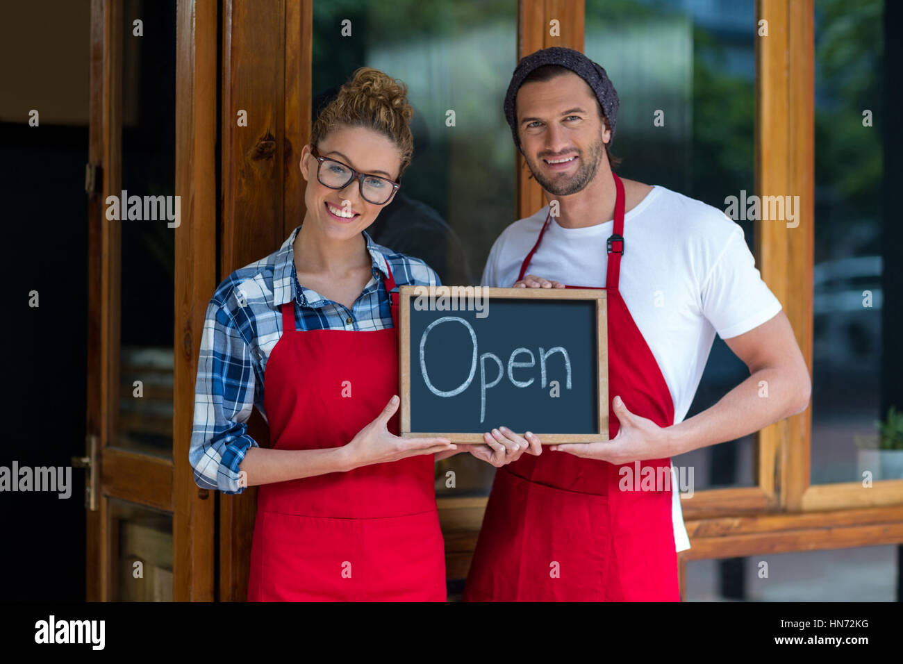 Portrait of smiling waitress and waiter standing with open sign board ...