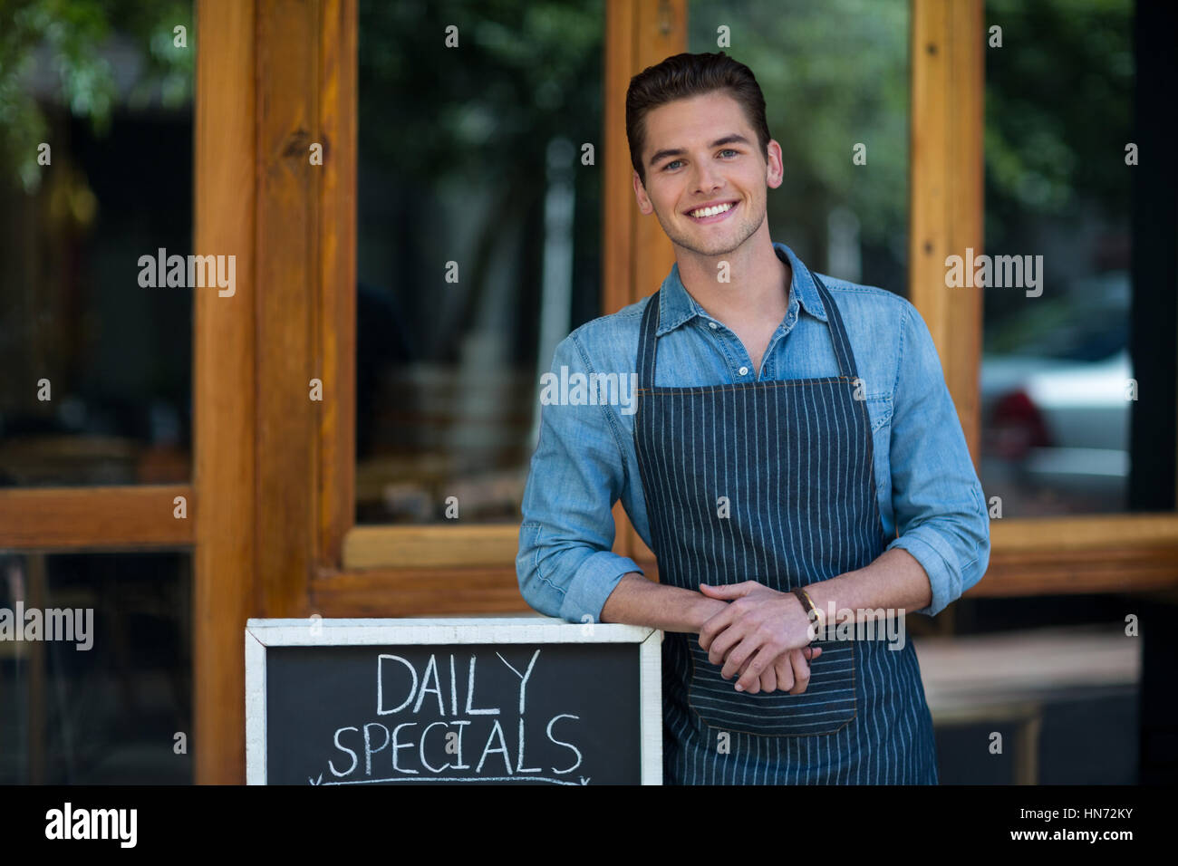 Portrait of smiling waiter leaning on menu board outside the cafe Stock ...