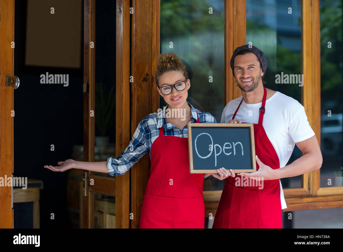 Portrait of smiling waitress and waiter standing with open sign board ...