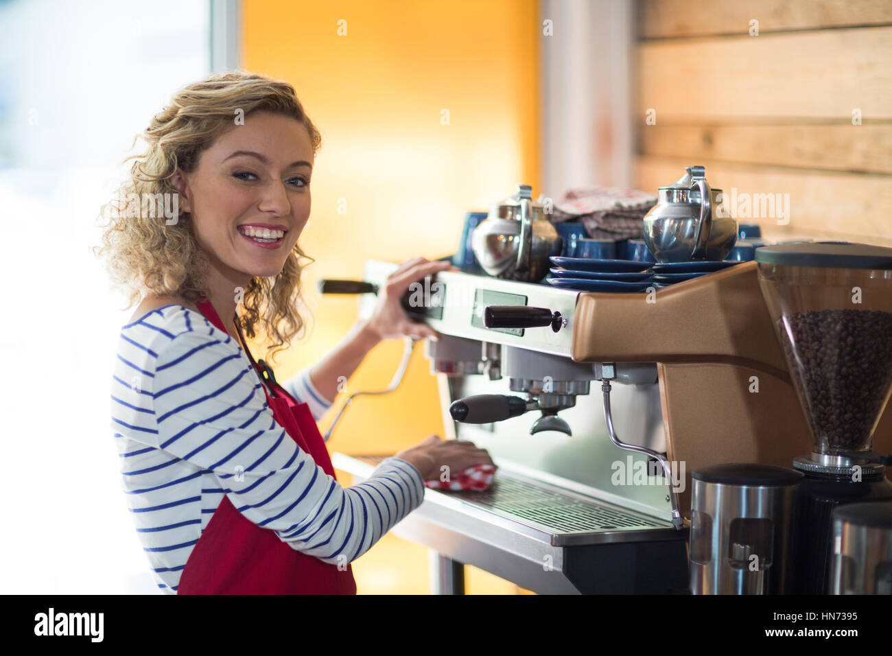Portrait of smiling waitress wiping espresso machine with napkin in ...