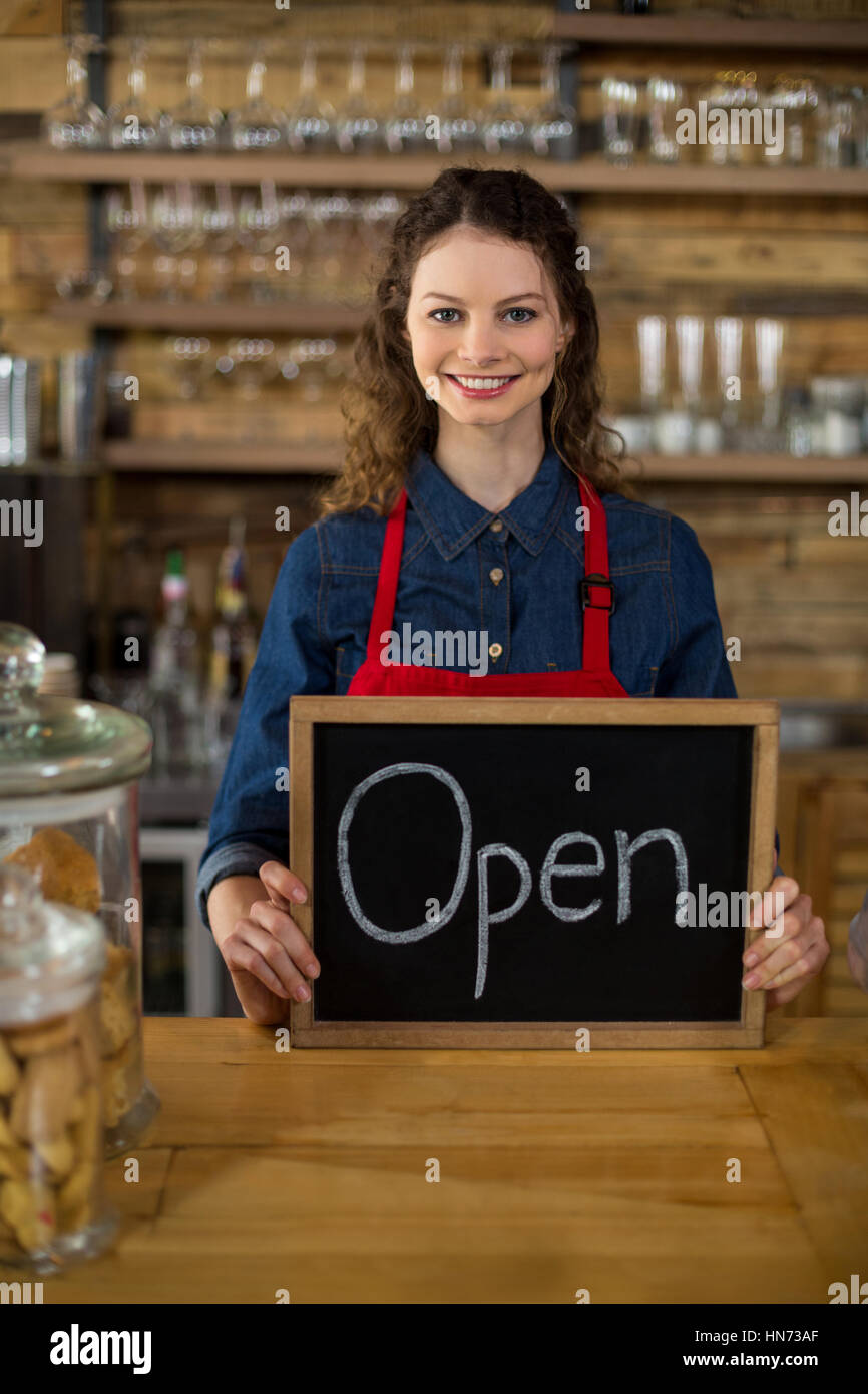 Portrait of smiling waitress showing chalkboard with open sign at ...