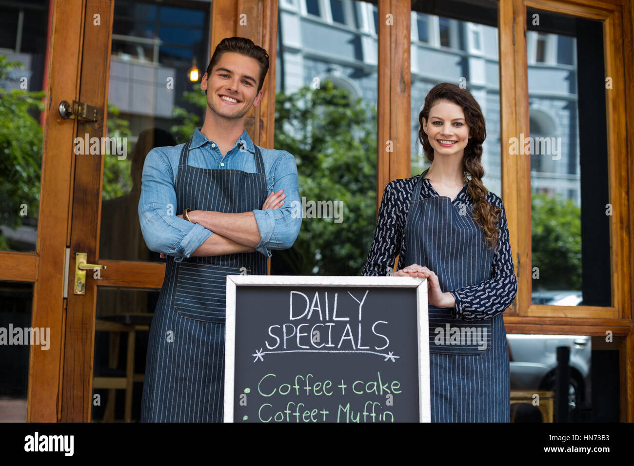 Smiling waiter and waitress standing with menu board outside the cafe ...