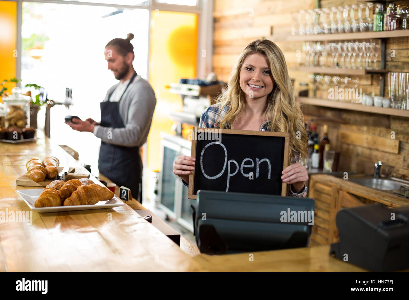 Smiling waitress standing at counter and showing slate with open sign ...