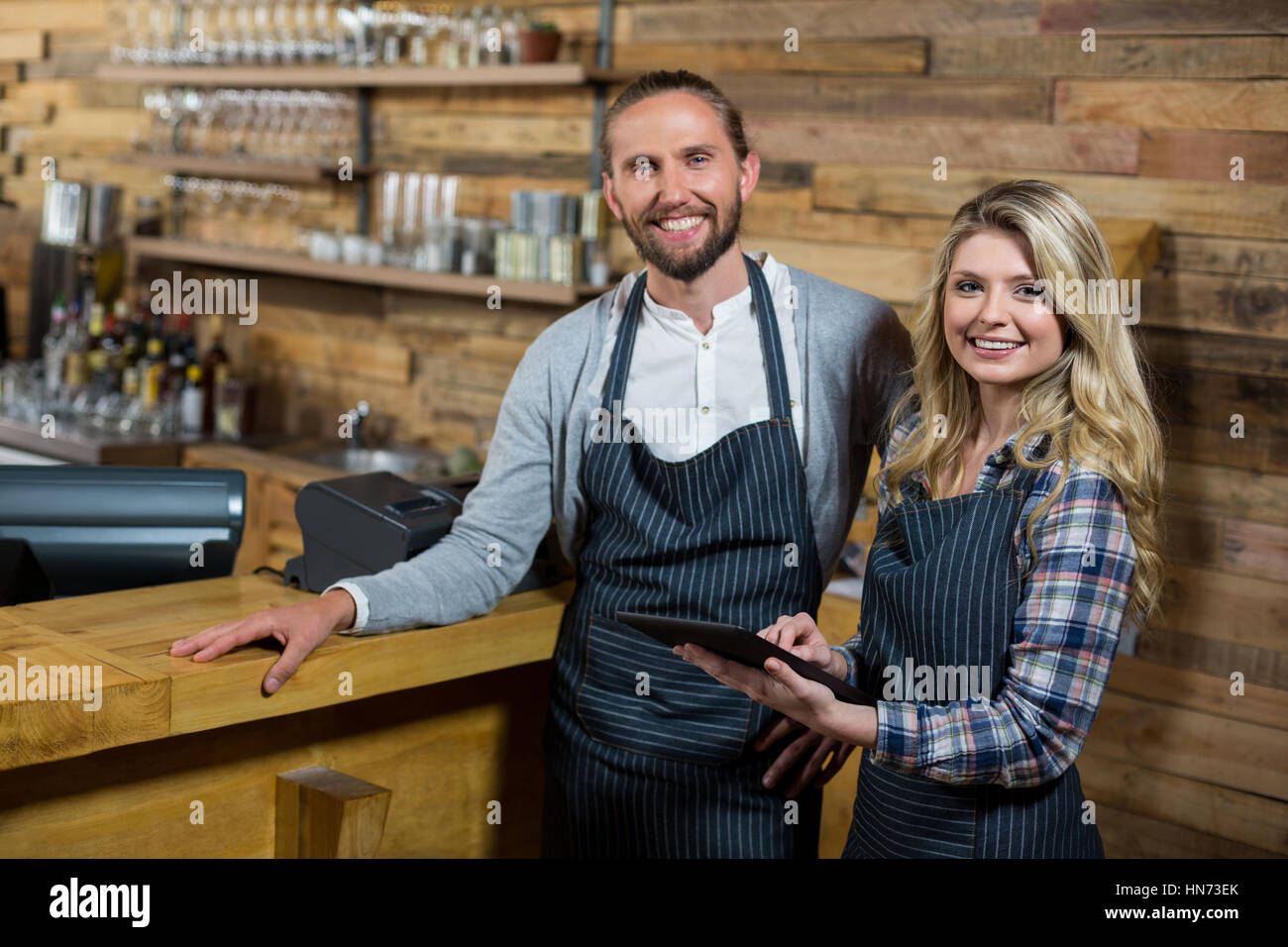 Portrait of smiling waiter and waitress using digital tablet at counter ...