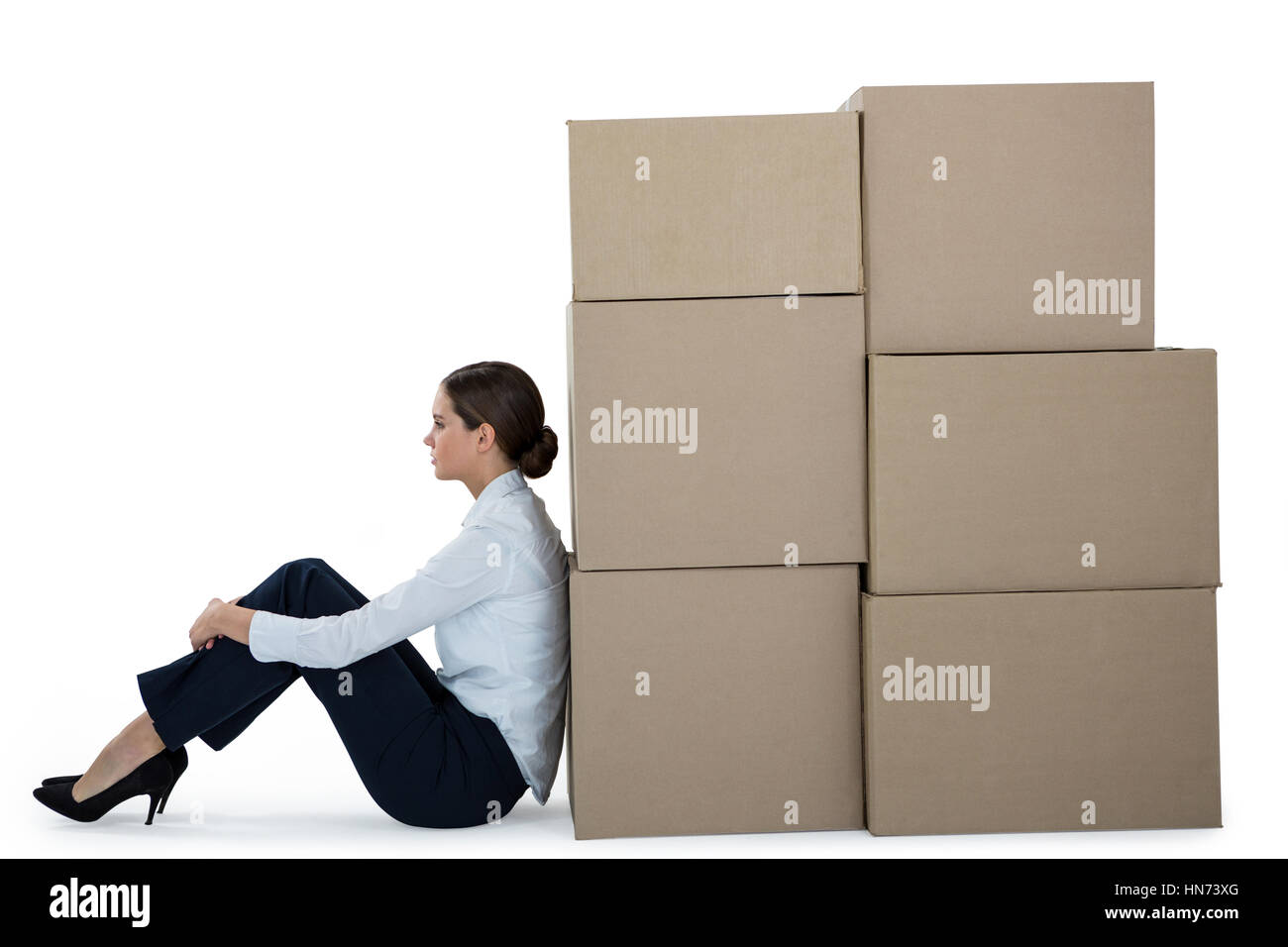 Thoughtful businesswoman leaning on cardboard boxes against white ...