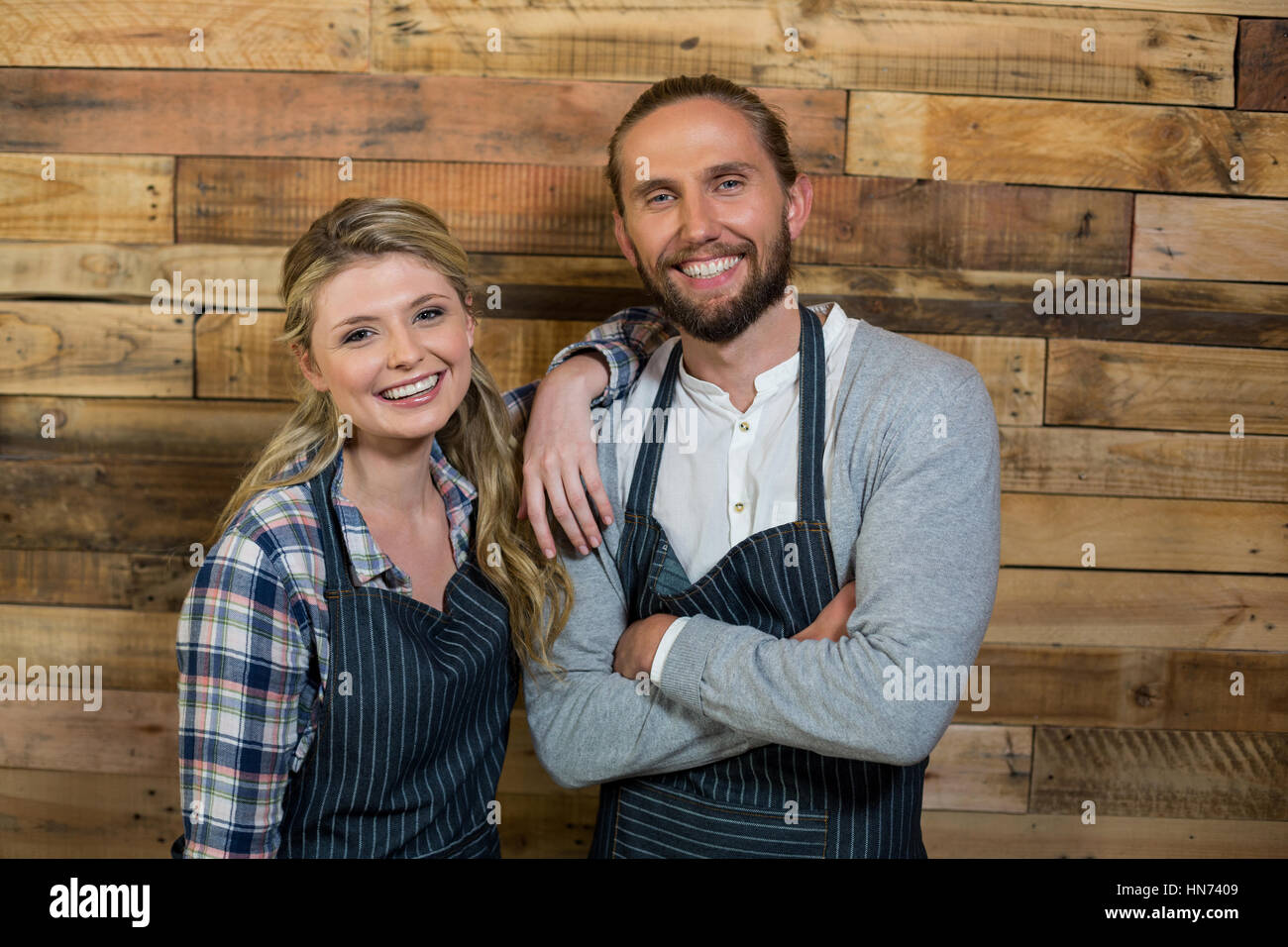 Portrait of smiling waiter and waitress standing against wooden wall in ...