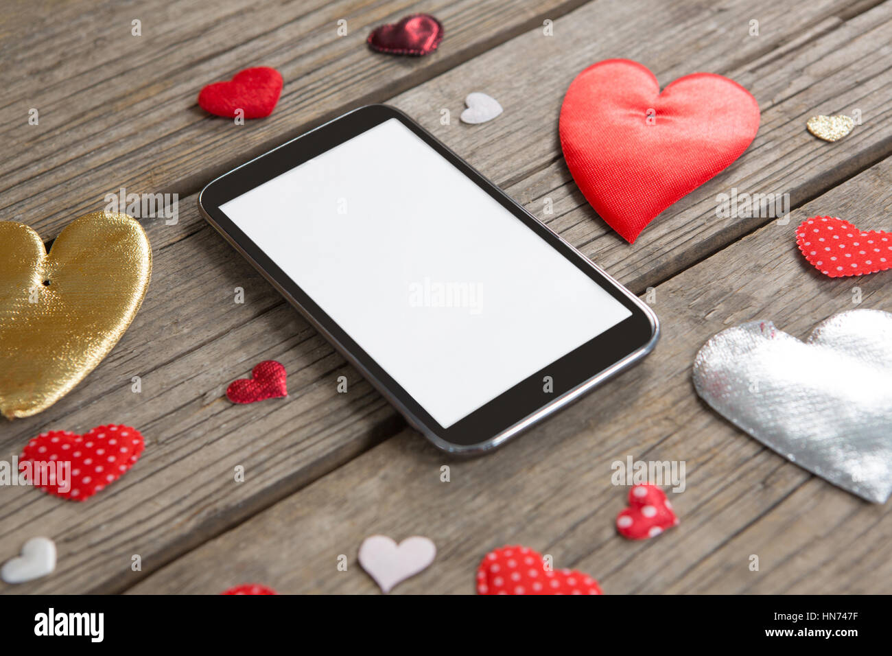 Mobile phone surrounded with heart shape decoration on wooden surface ...