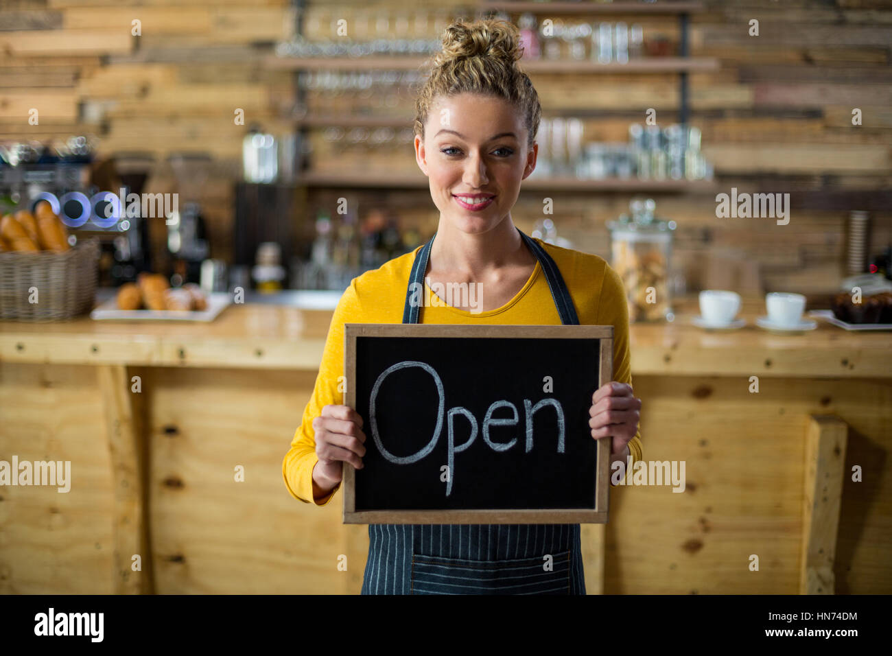 Portrait of smiling waitress standing with open sign board in cafe ...