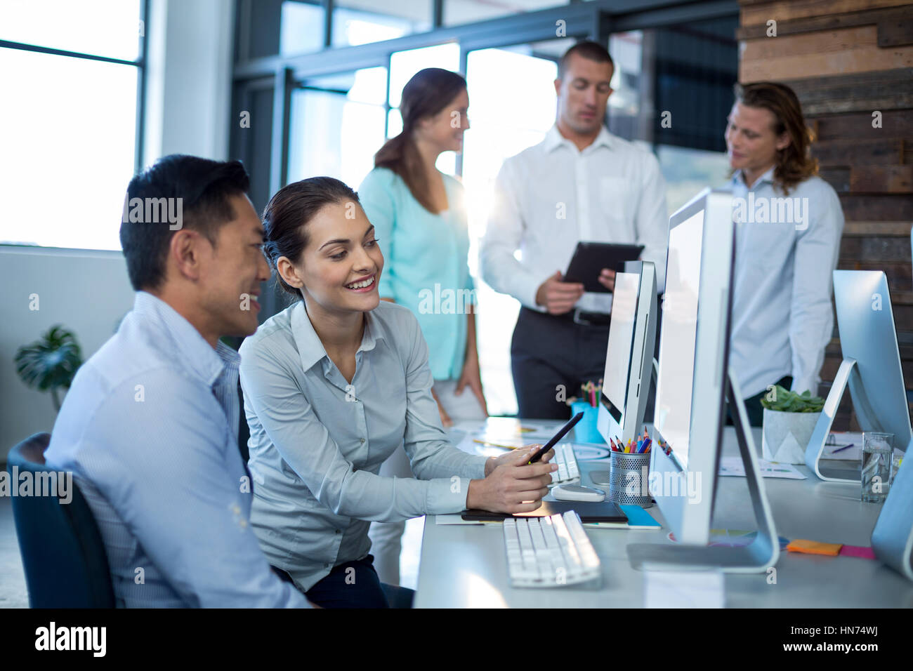 Businesspeople interacting while working on personal computer in office ...