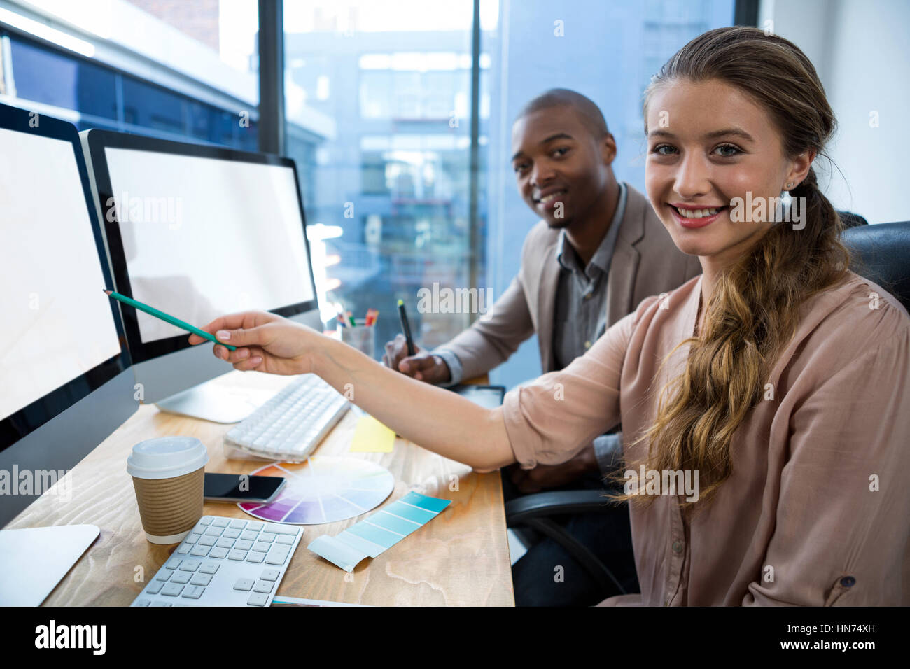 Portrait of graphic designer at desk with colleague in office Stock ...