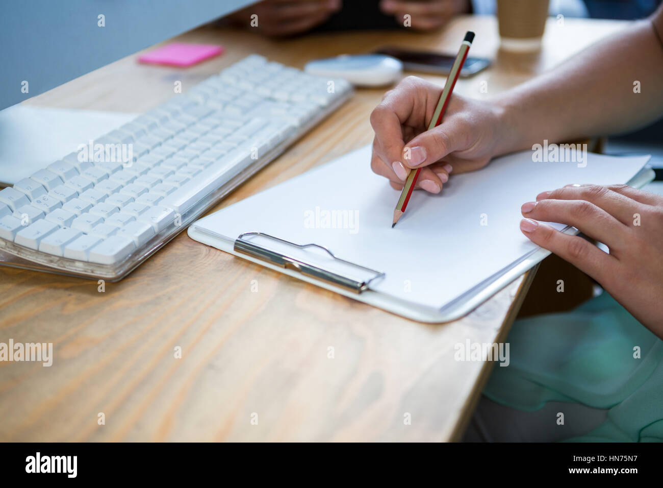 Close-up of female business executive writing on clipboard at desk in ...