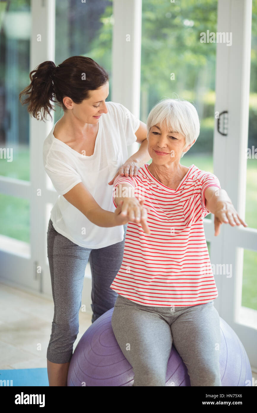 Female coach assisting senior woman in performing exercise at home ...